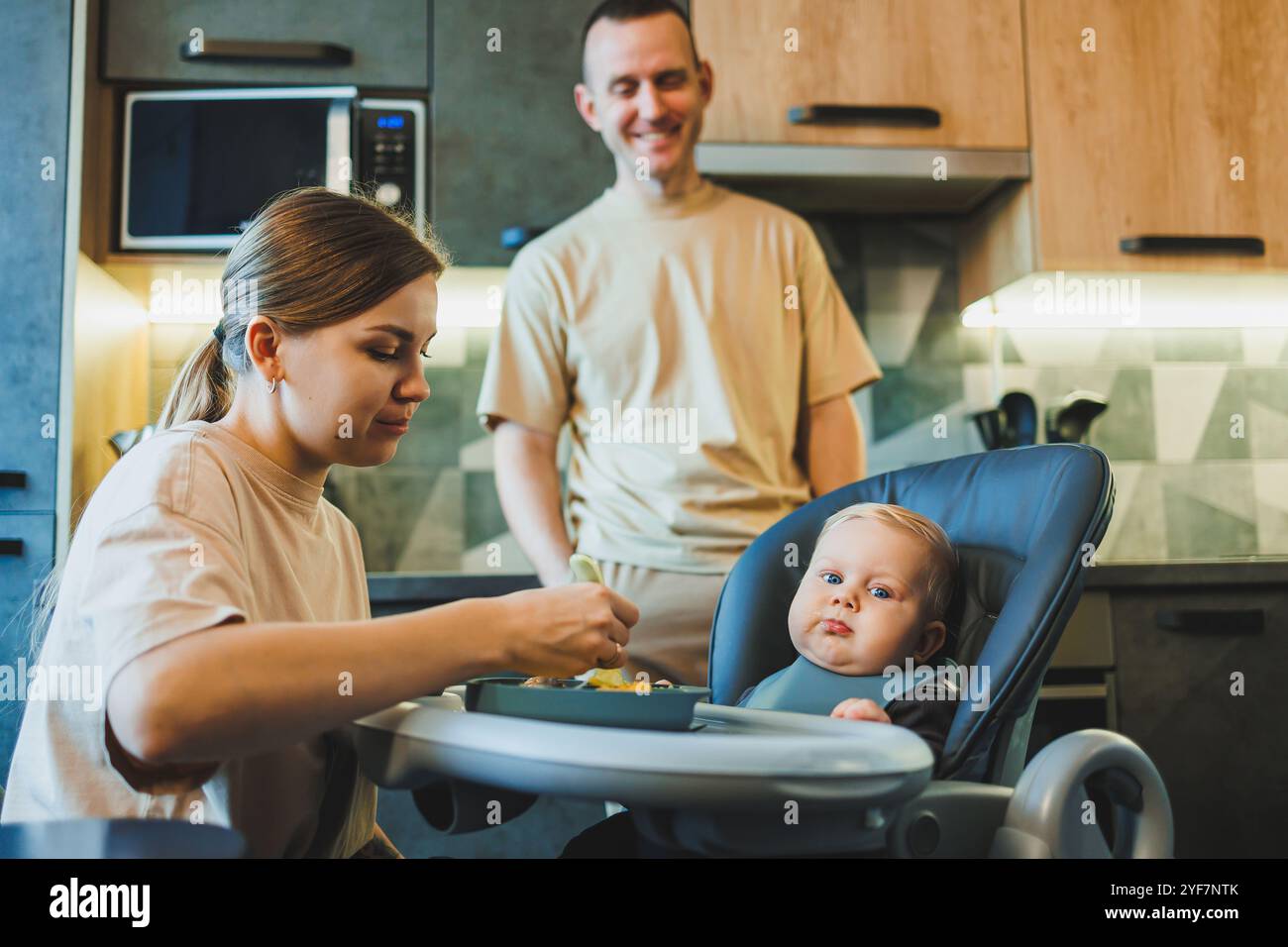 Young parents, mom and dad, feed the baby with complementary food for ...
