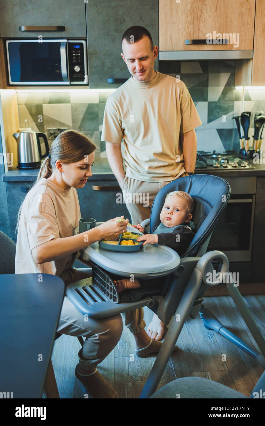 Young parents, mom and dad, feed the baby with complementary food for ...