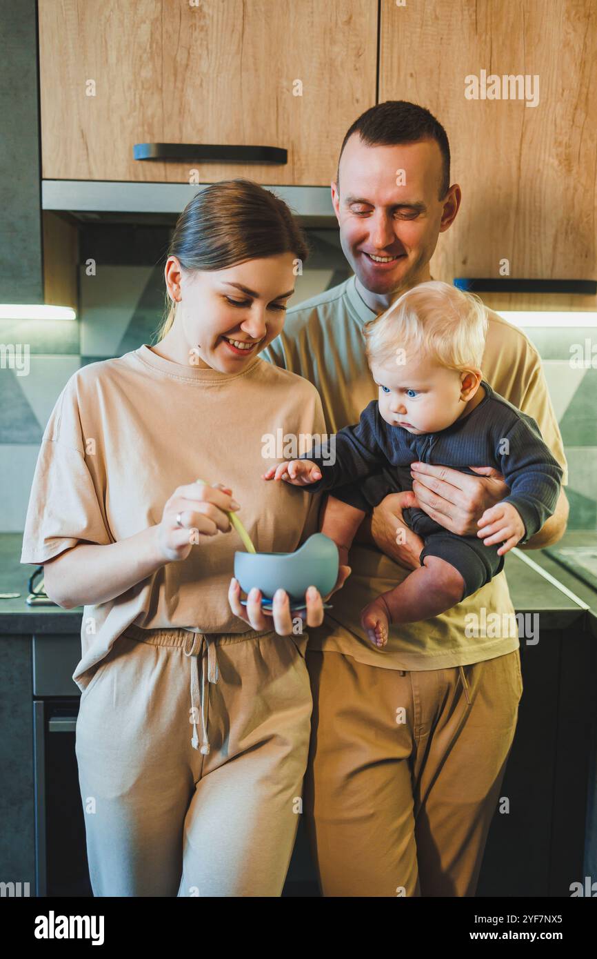 Young parents, mom and dad, feed the baby with complementary food for ...