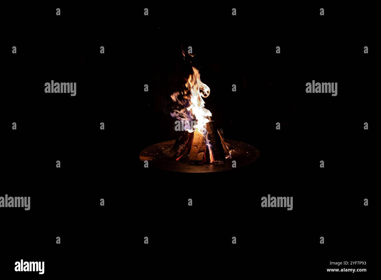 A campfire burns brightly in a circular metal fire pit, with logs in a ...