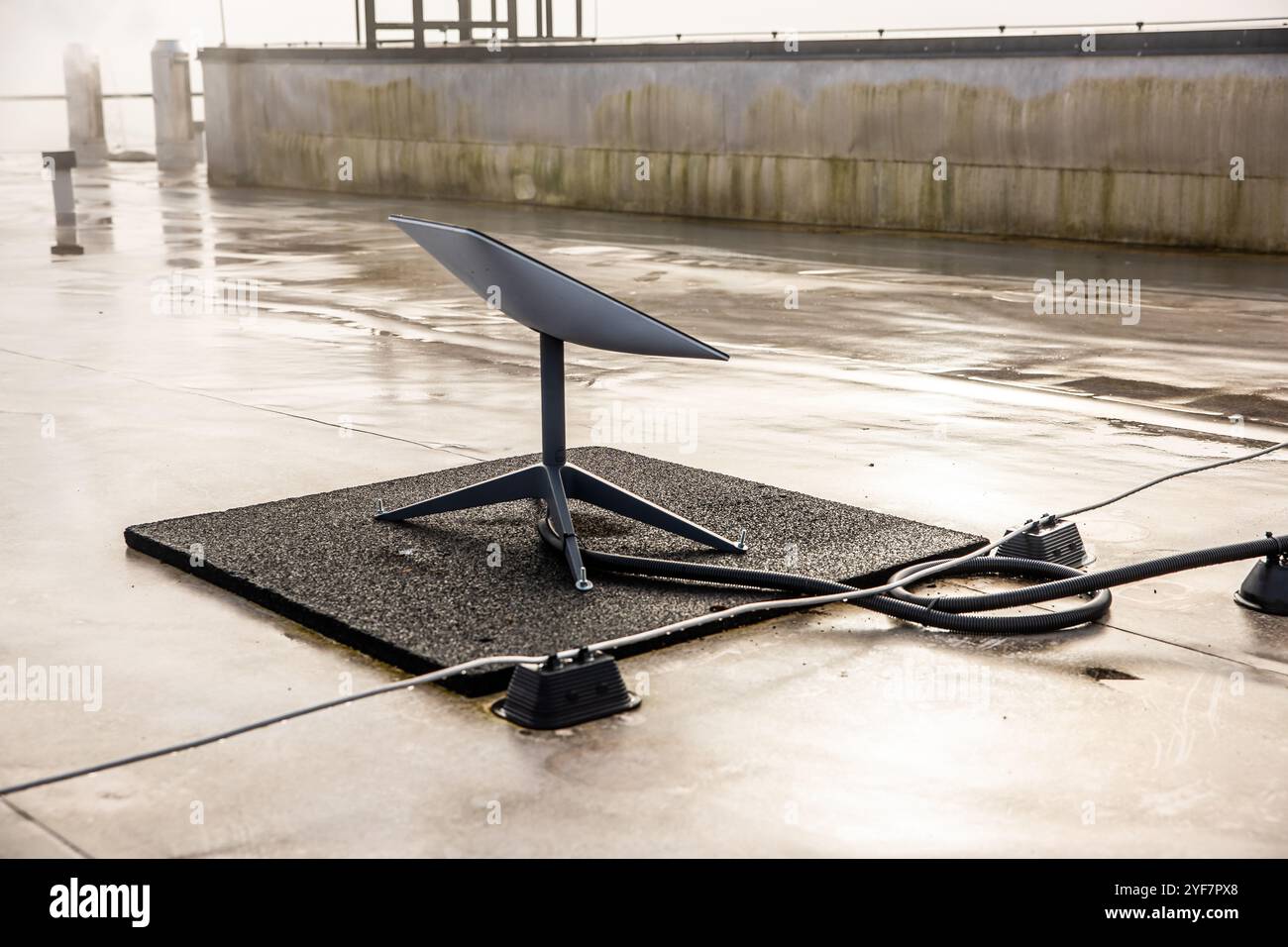 A Starlink satellite dish is mounted on a wet rooftop, with cables ...