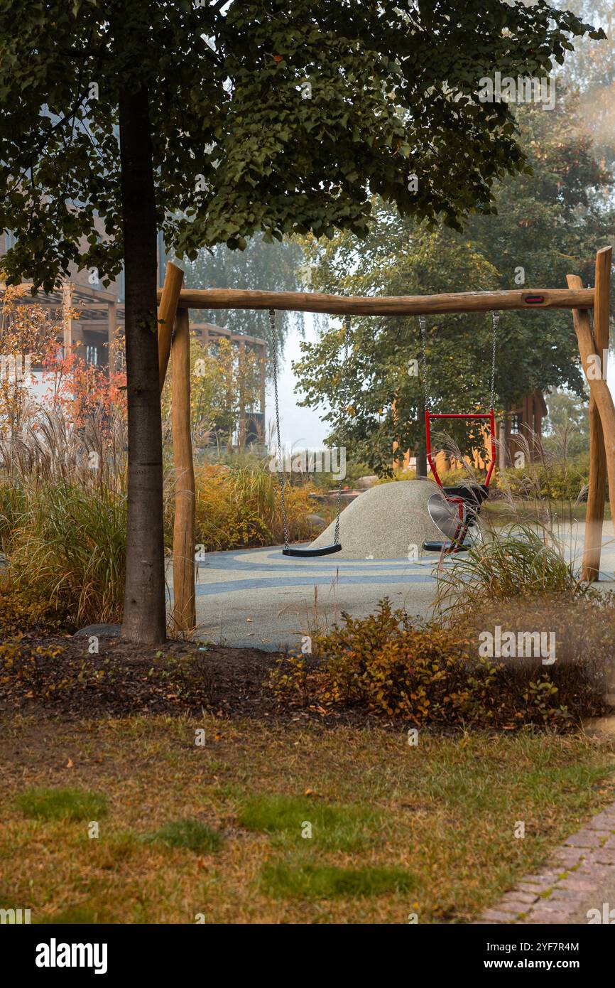 A playground features a wooden swing set and sand mound, surrounded by ...