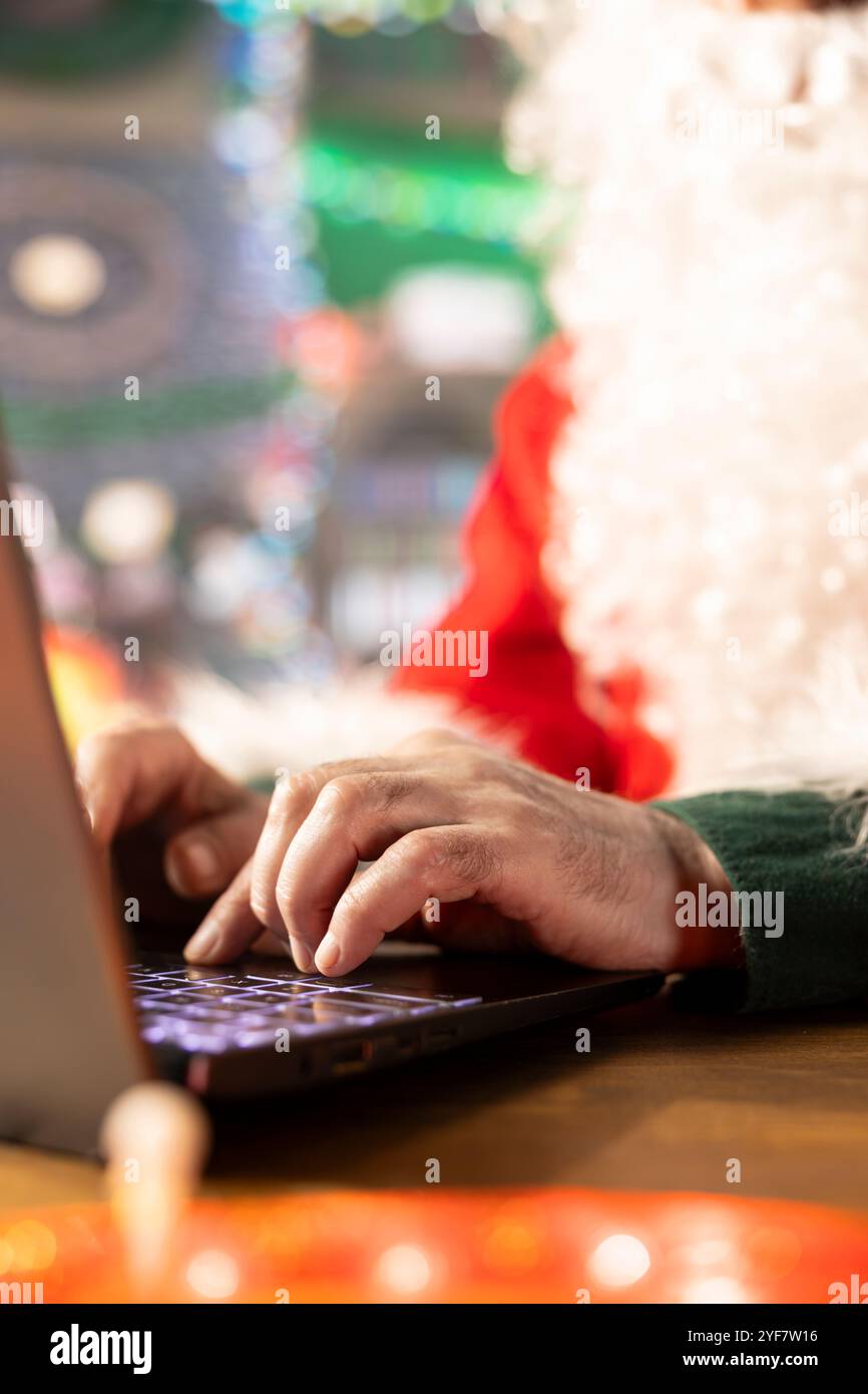 Santa Claus uses a laptop in his festive log cabin navigating online ...
