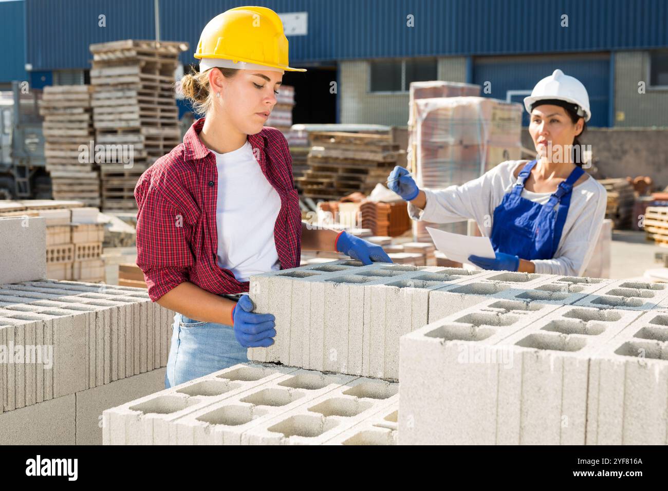 Female builders with hollow concrete blocks in outdoor warehouse Stock ...