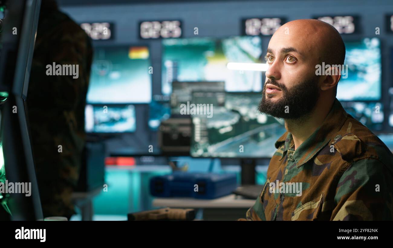 Military soldier in mission control center overseeing national safety operations with devices ...