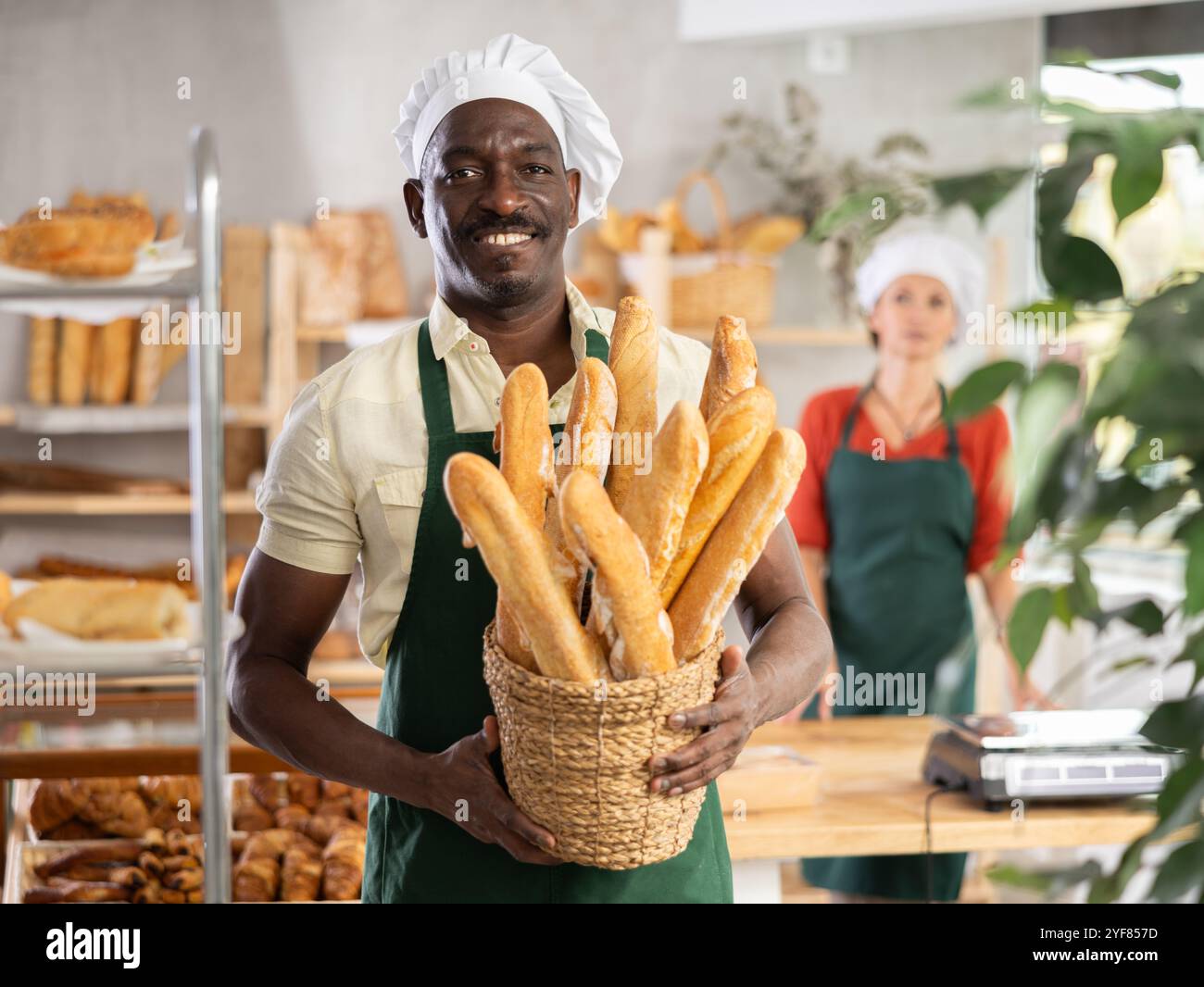 African male baker worker sells baguette, shows many products Stock ...