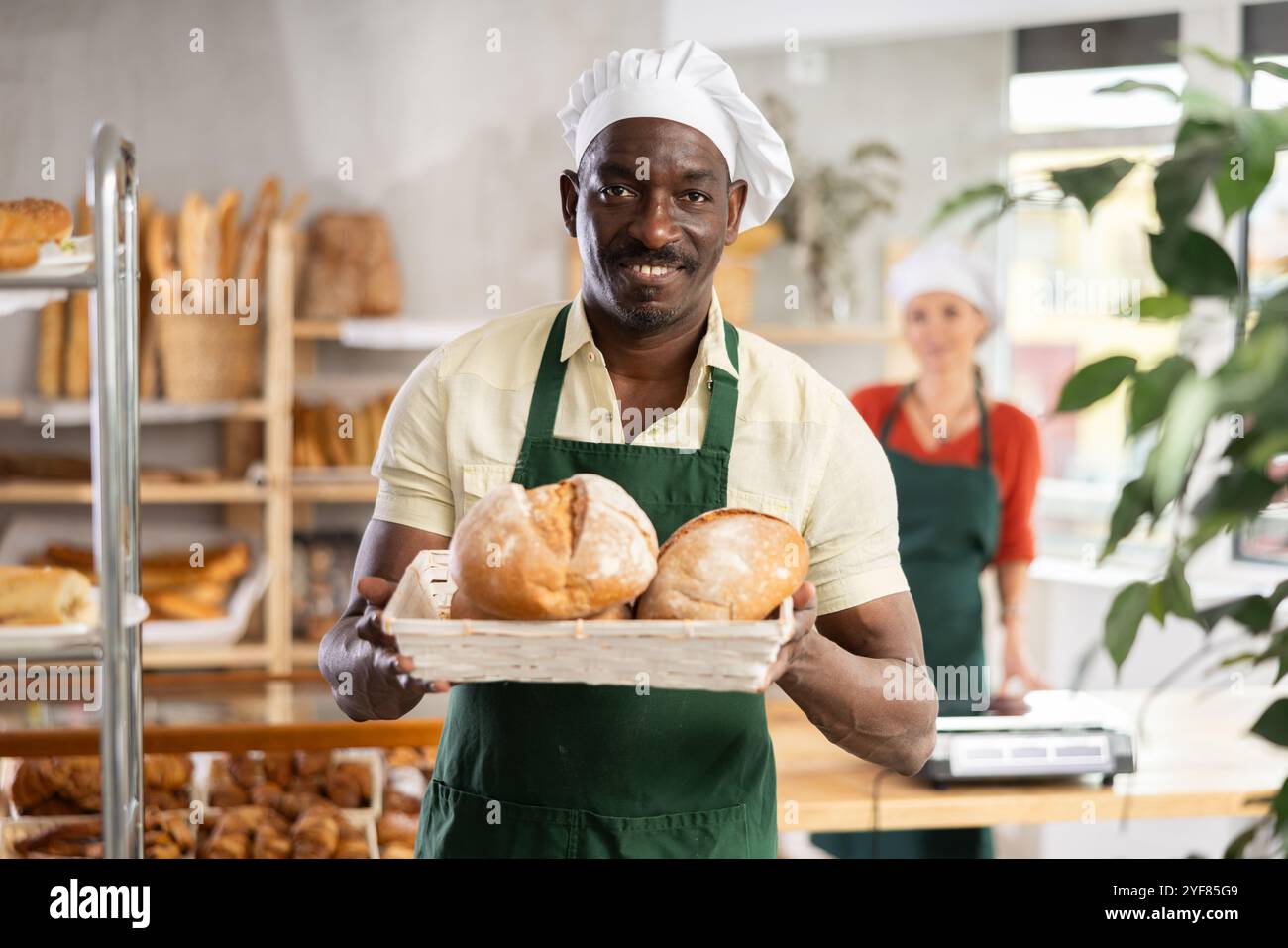 Portrait of male baker with bread and baguettes in hands in bakery ...