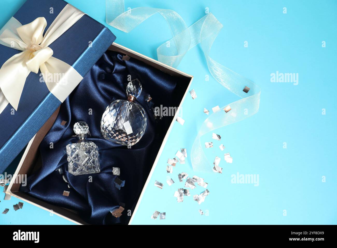 Perfume bottles in gift box and confetti on light blue background, top ...