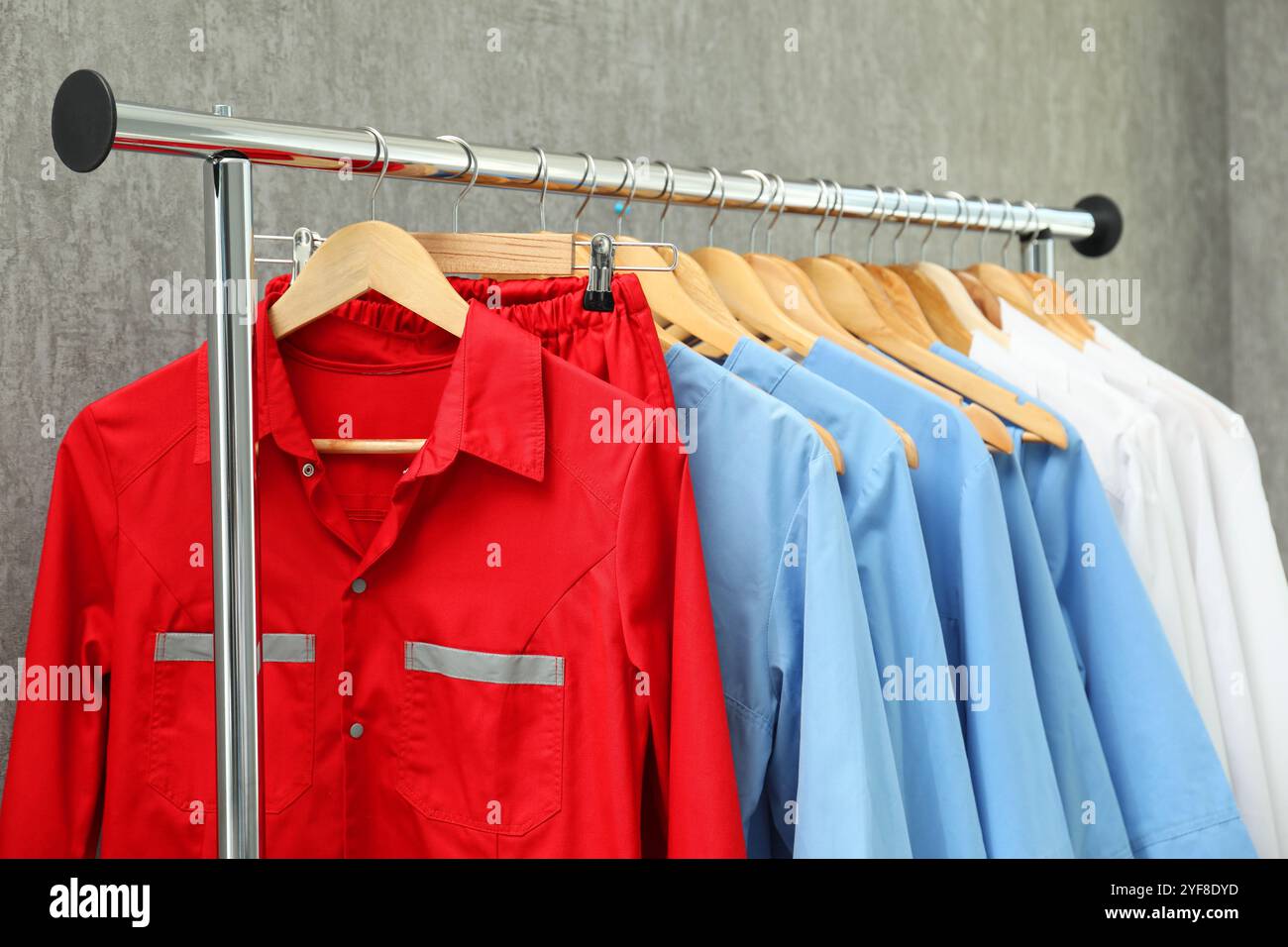 Different medical workers' uniforms on clothing rack against grey ...