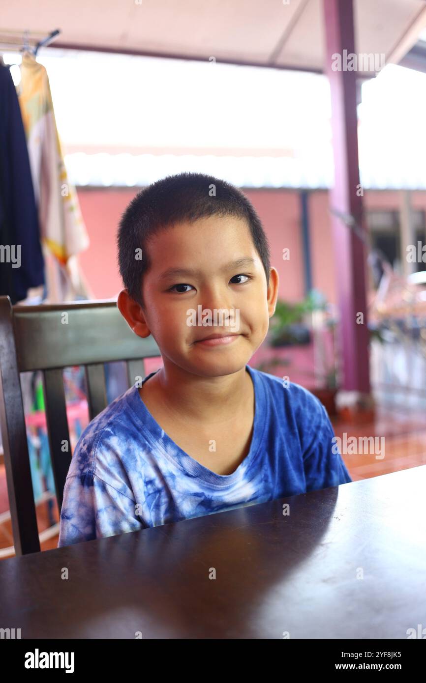 A cheerful young boy sits at a table, displaying a warm smile. His ...