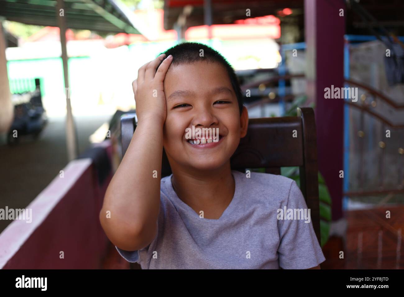 A cheerful boy sitting outdoors with a joyful smile, playfully resting ...