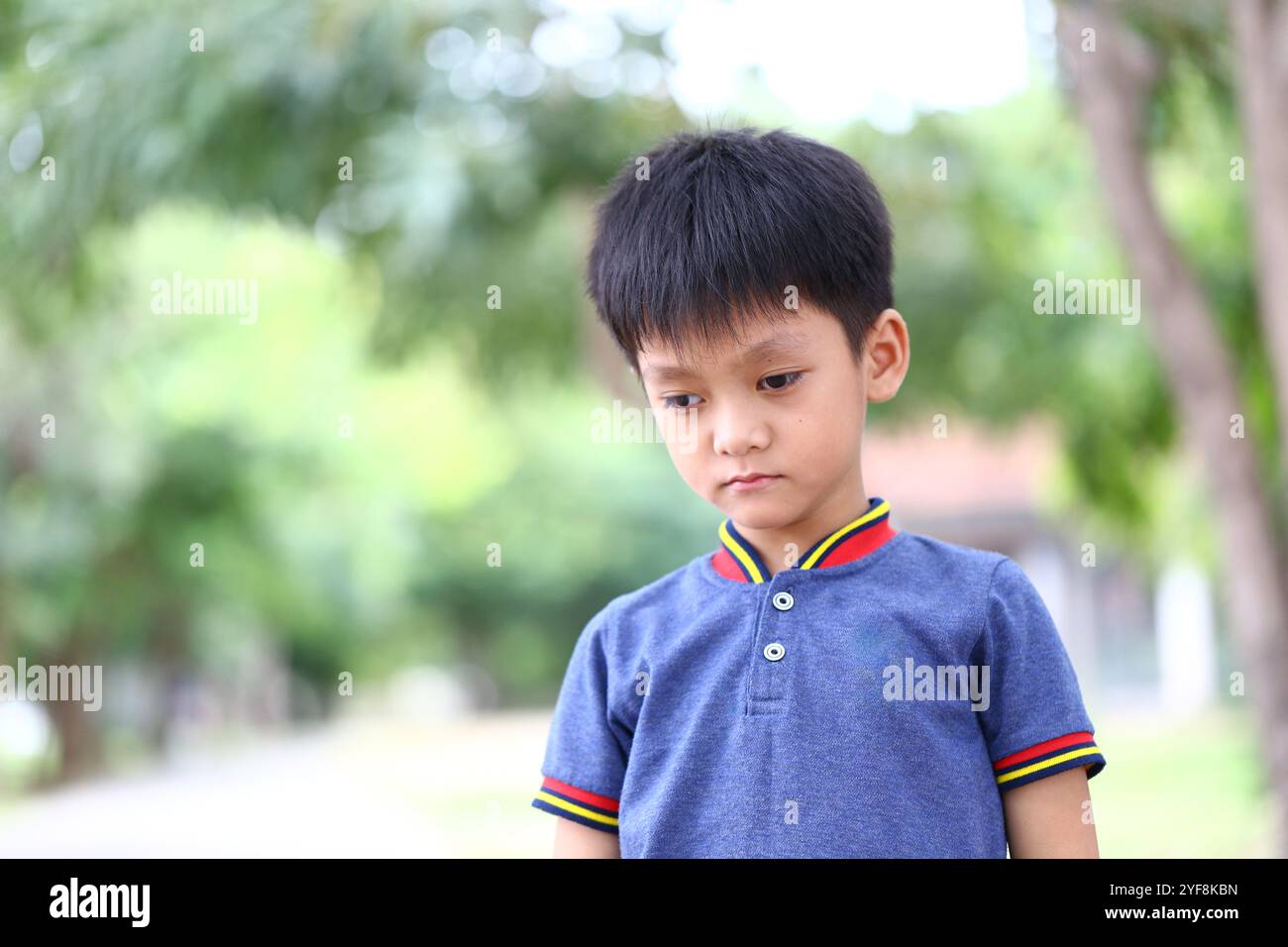 A young boy stands outdoors, looking down with a contemplative ...