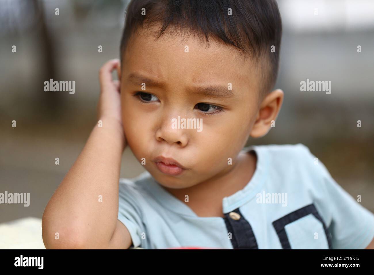 A young boy displays a thoughtful expression while pondering outdoors ...