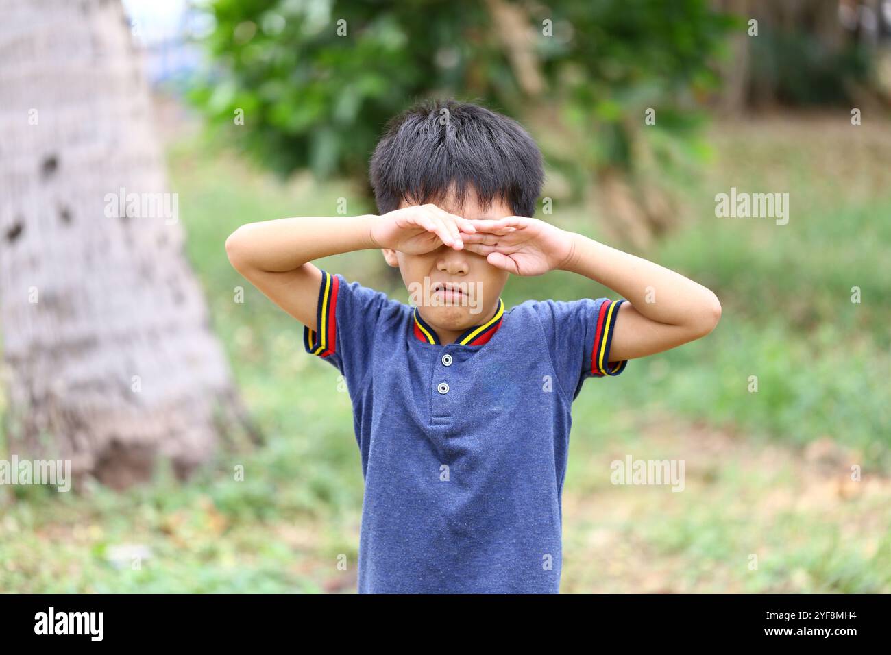 A young child stands outside, shielding his eyes from the bright ...