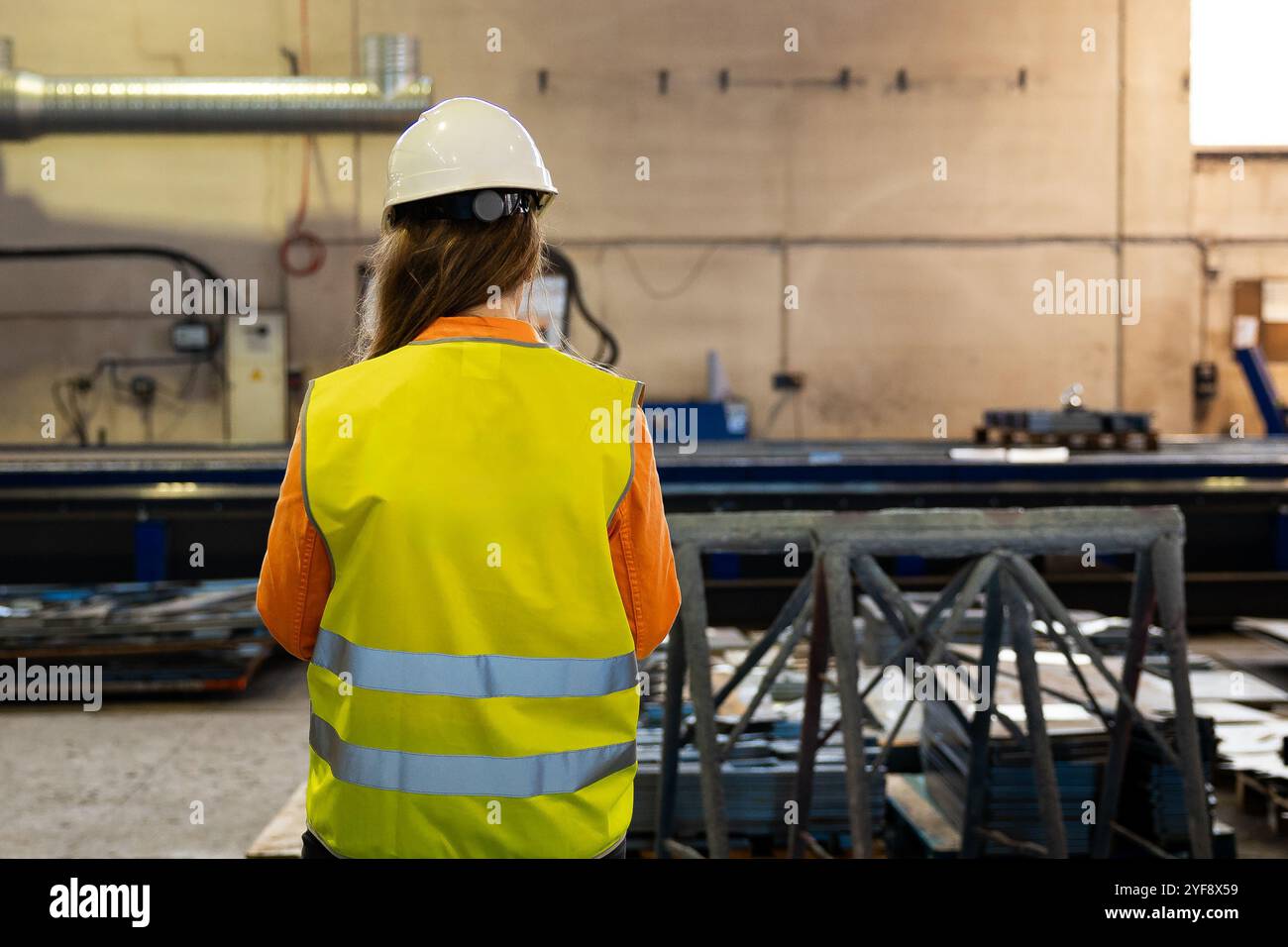 Rear view of an industrial woman engineer with smartphone in a factory ...