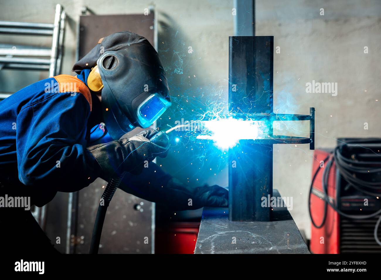 Welding work at a metalworking plant. A helmeted welder welds a metal ...