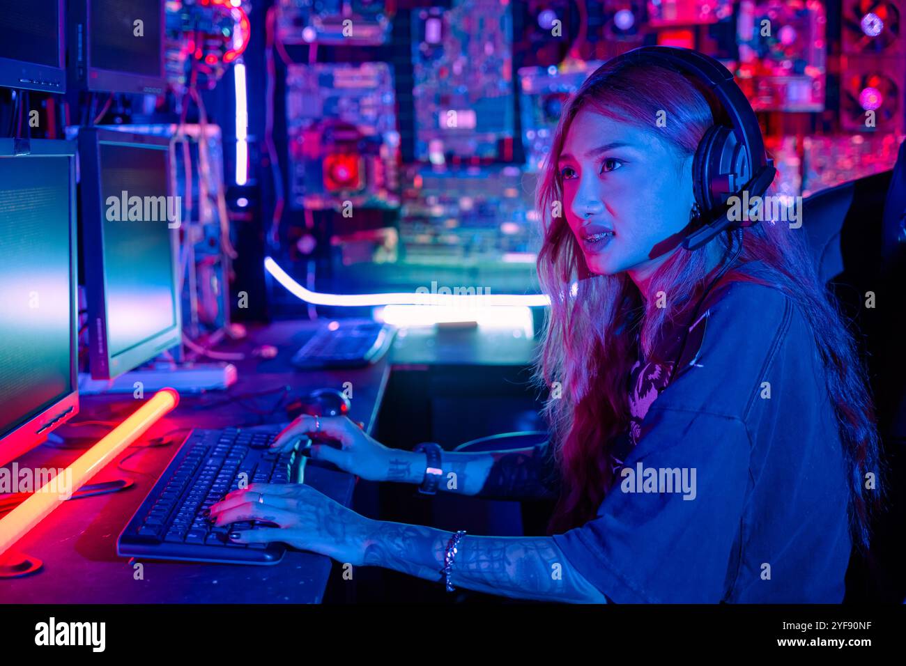 Woman hacker sitting in front of a computer typing on keyboard hacking servers in neon light ...