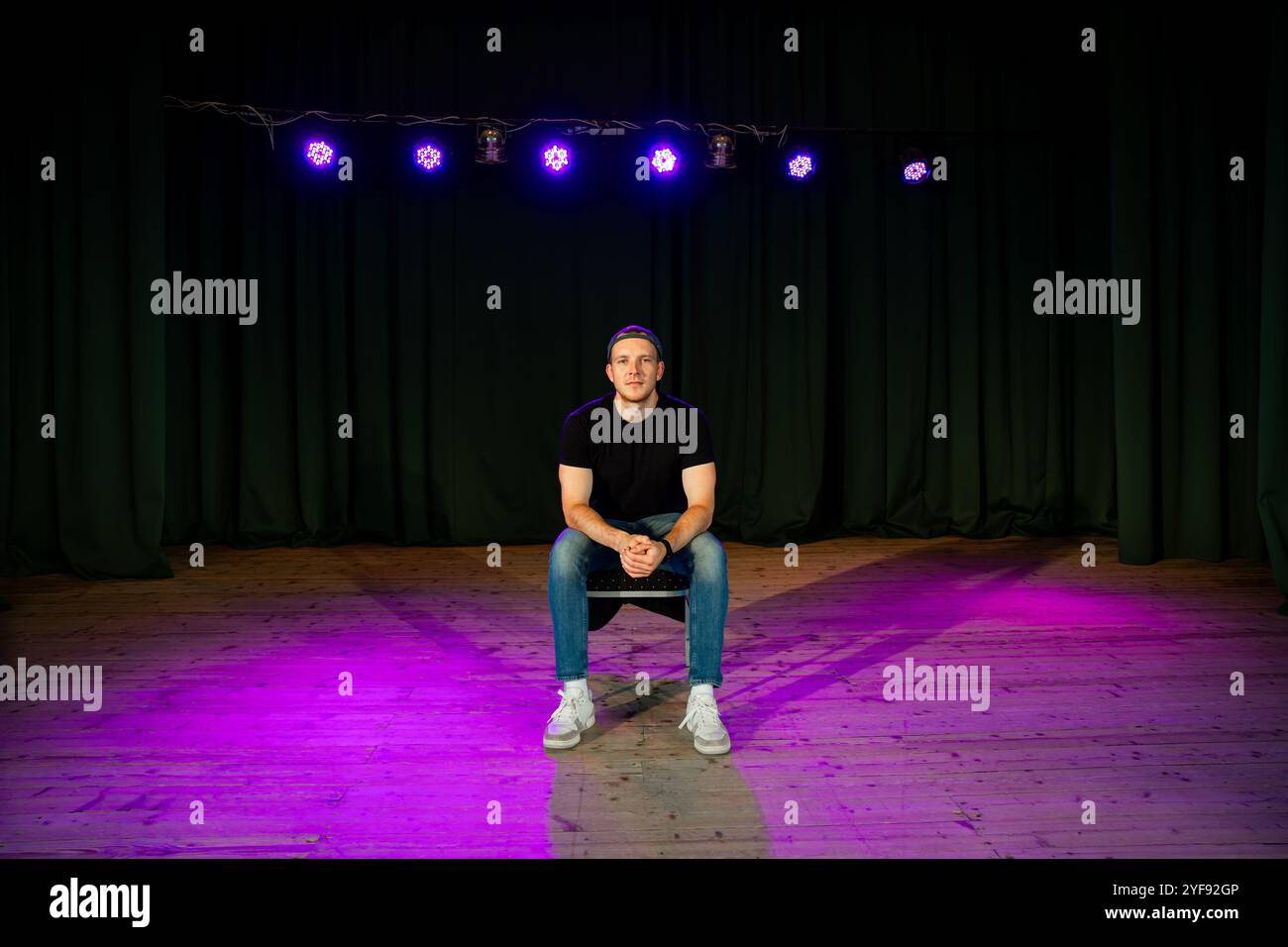 aspiring actor sitting center stage under spotlights, contemplating his ...
