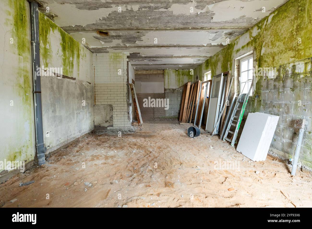 Abandoned building interior in disrepair with debris, exposed pipes, and missing doors awaiting ...