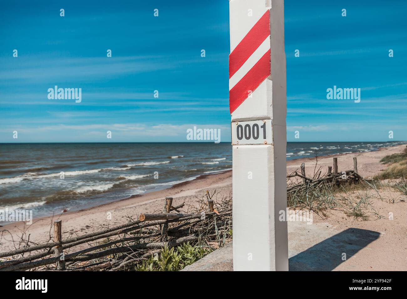 Red and white striped border post marked '0001' on a sunny beach ...