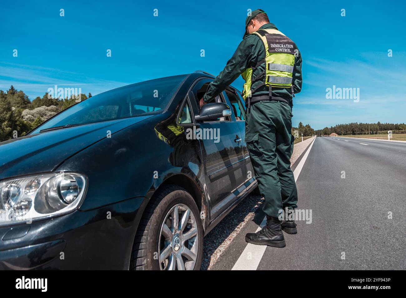 border patrol officer inspecting vehicle at checkpoint on sunny day ...