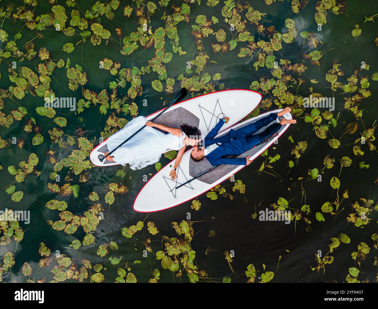 aerial view of a couple in wedding attire lying on a paddleboard amidst ...