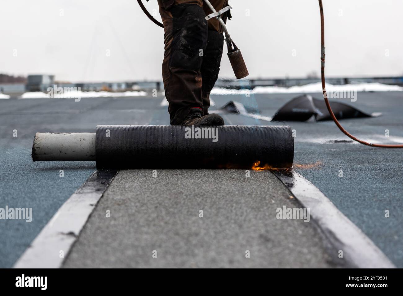 professional roofer at work securing rolled tar paper with a blowtorch ...