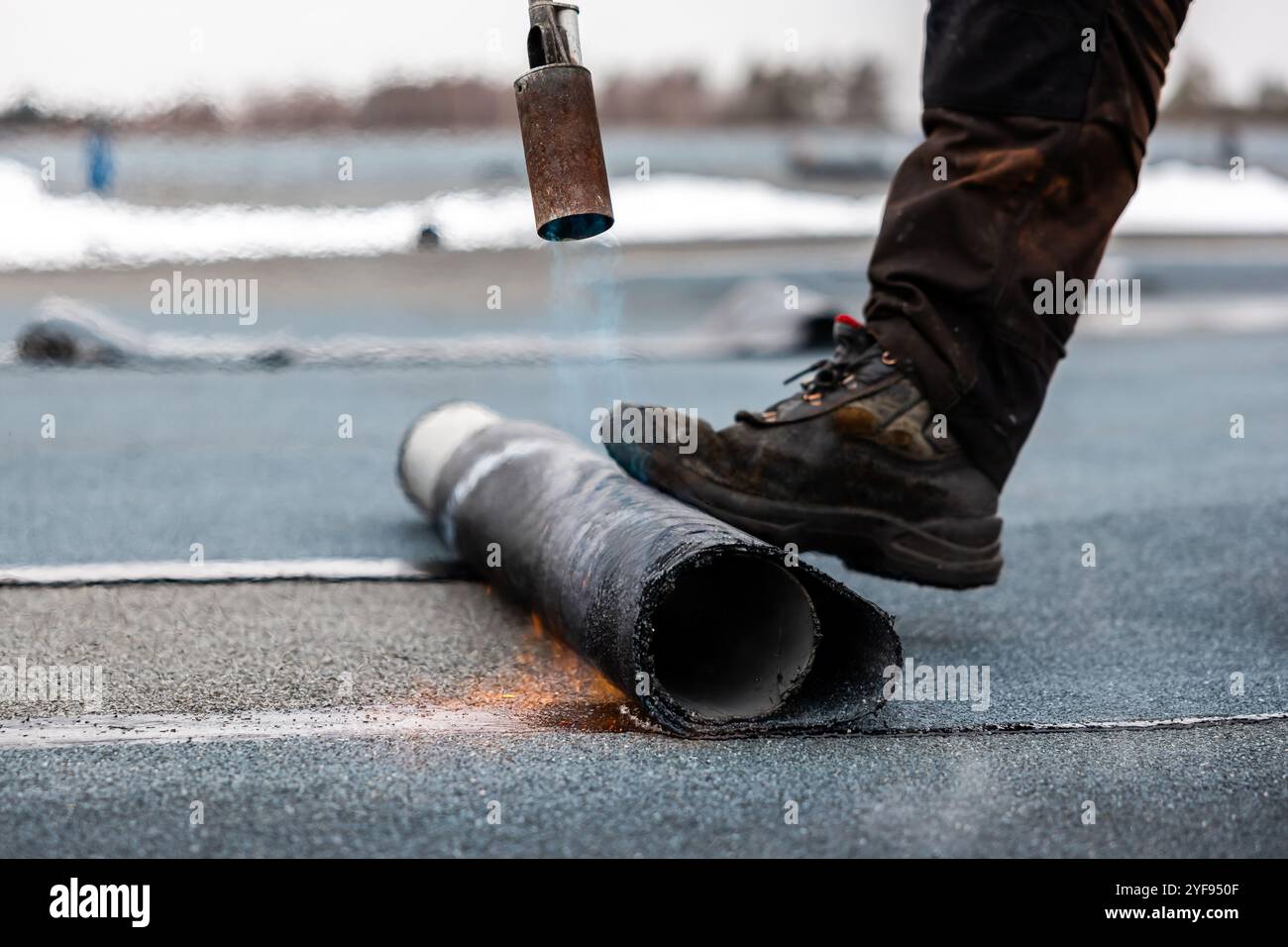 professional roofer at work securing rolled tar paper with a blowtorch ...