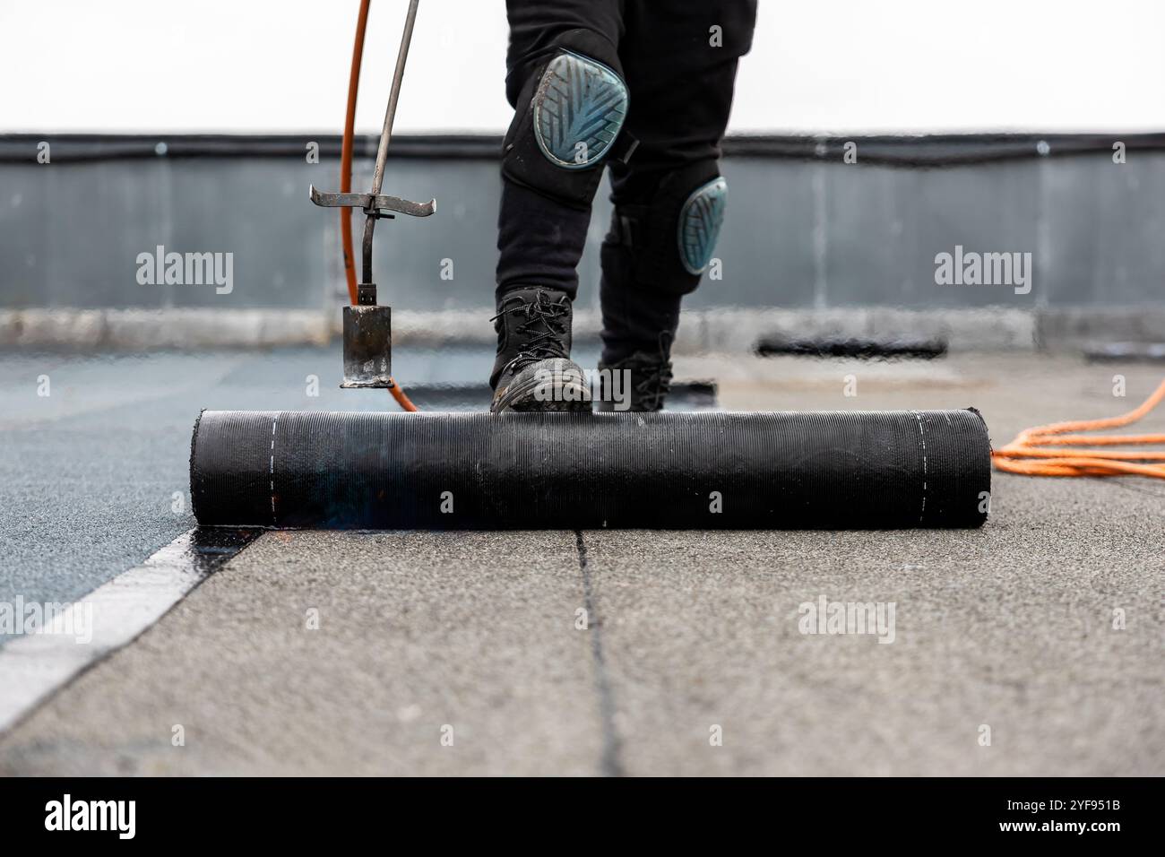 professional roofer applying bitumen roll on flat roof with a gas ...