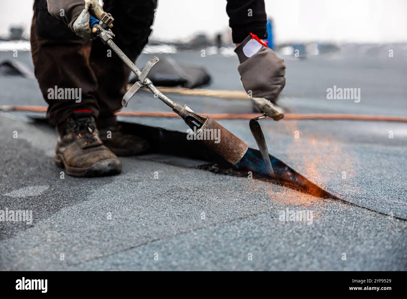 professional roofer applying bitumen roll on flat roof with a gas ...