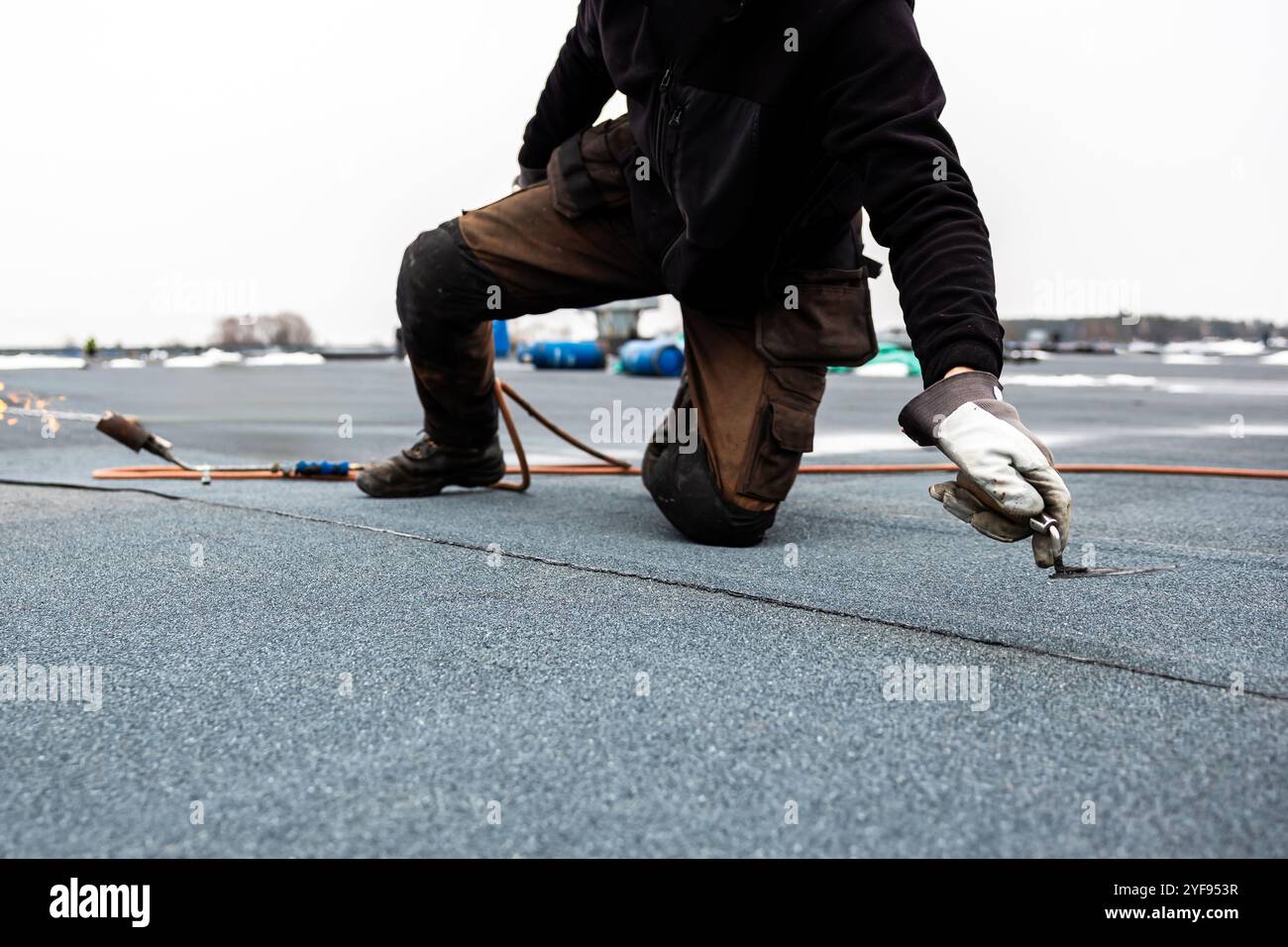professional roofer applying bitumen roll on flat roof with a gas ...