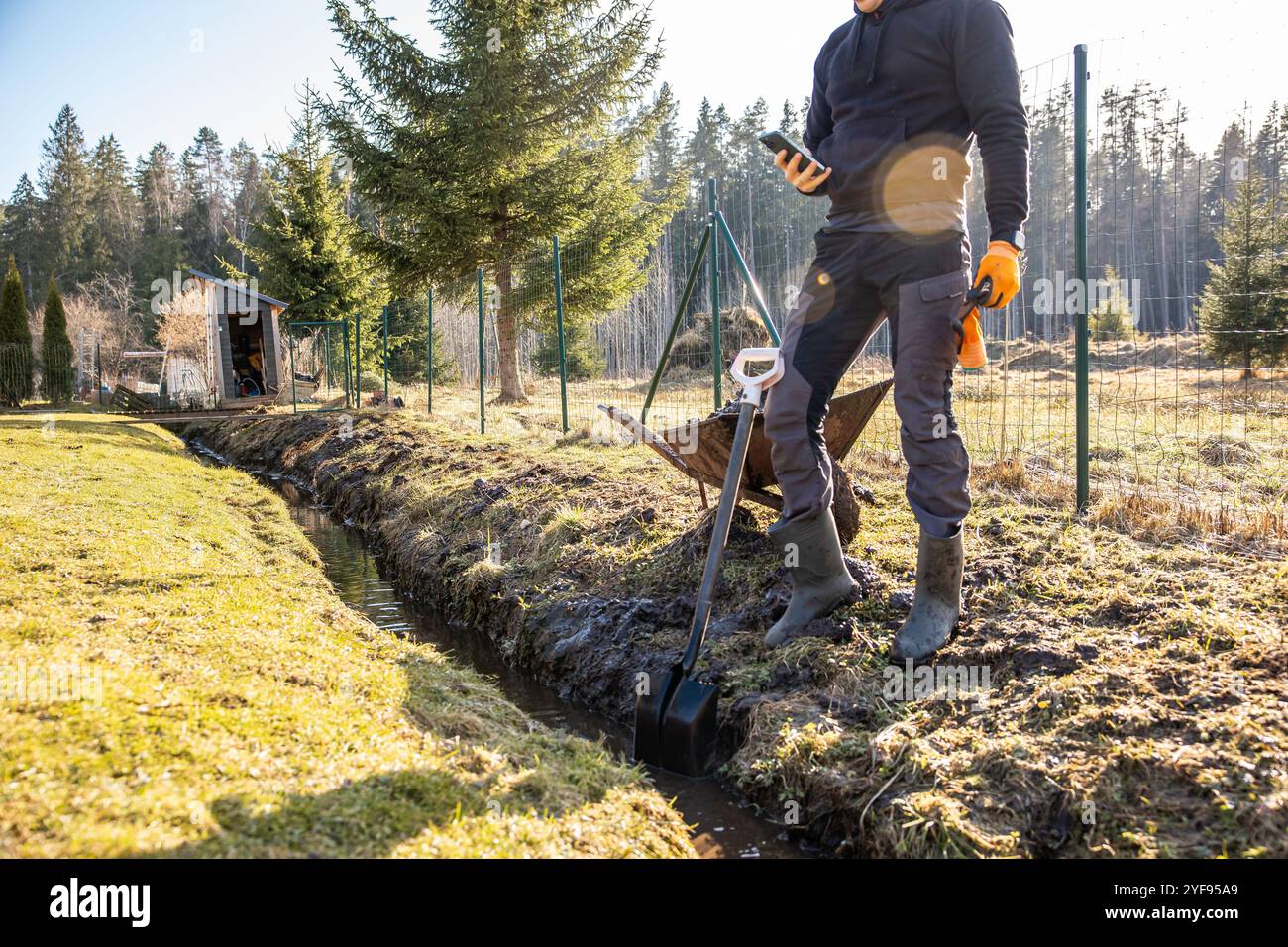 Man pausing from outdoor work to check his phone while kneeling by a ...