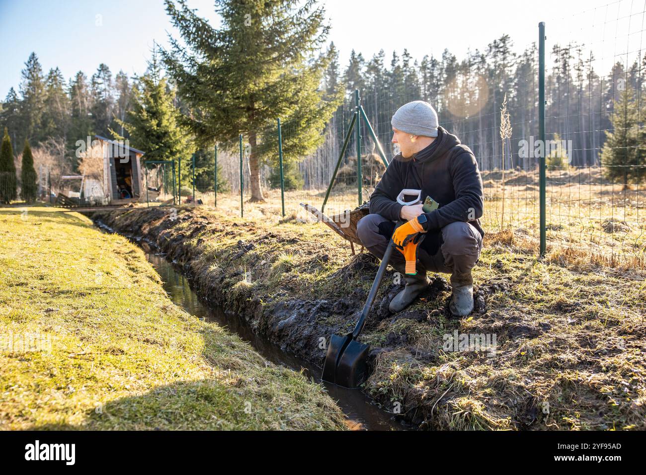 Man pausing from outdoor work to check his phone while kneeling by a ...