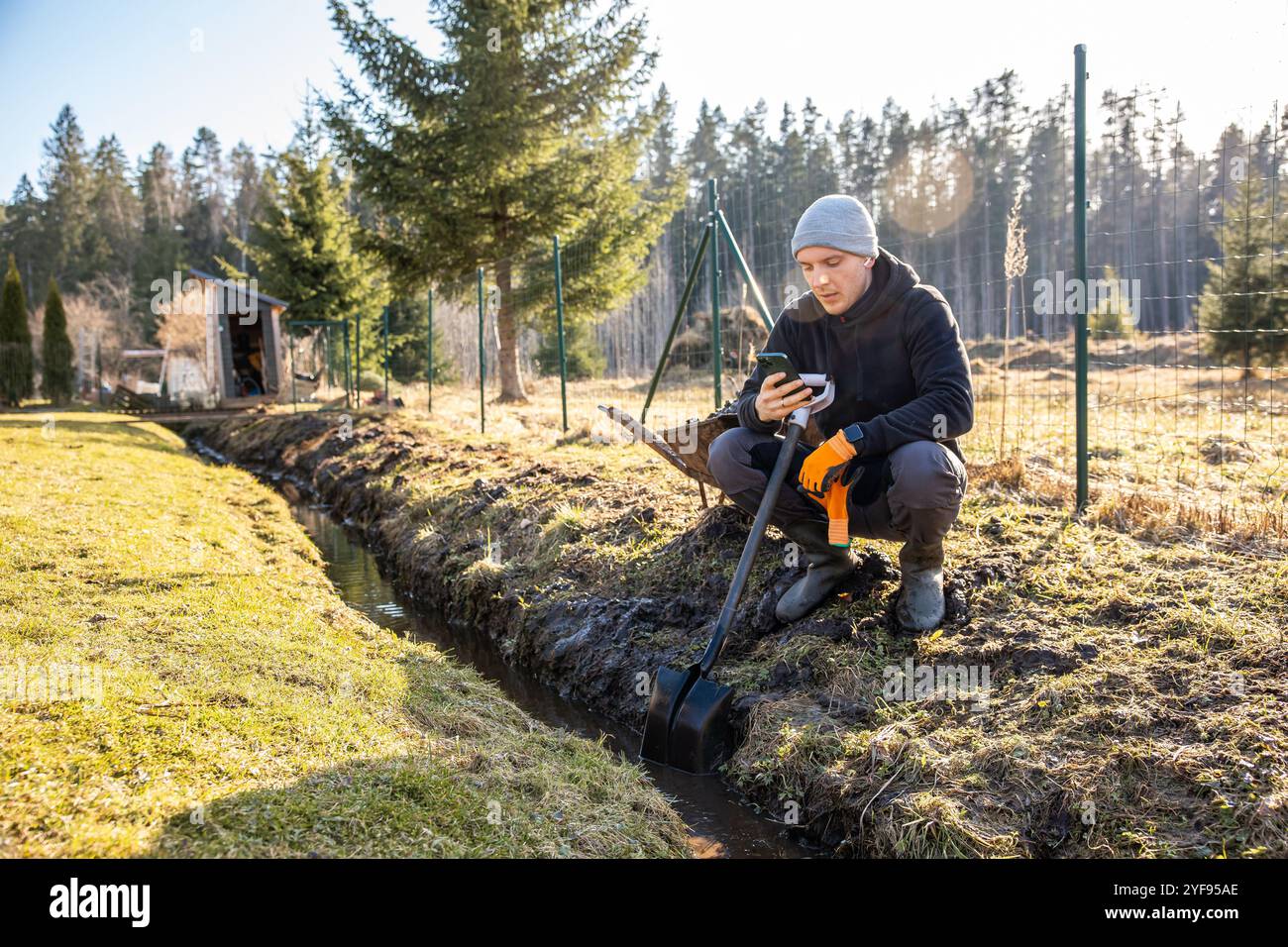 Man pausing from outdoor work to check his phone while kneeling by a ...