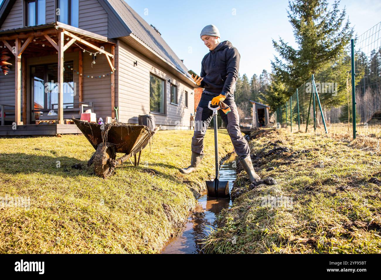 Man pausing from outdoor work to check his phone while kneeling by a ...