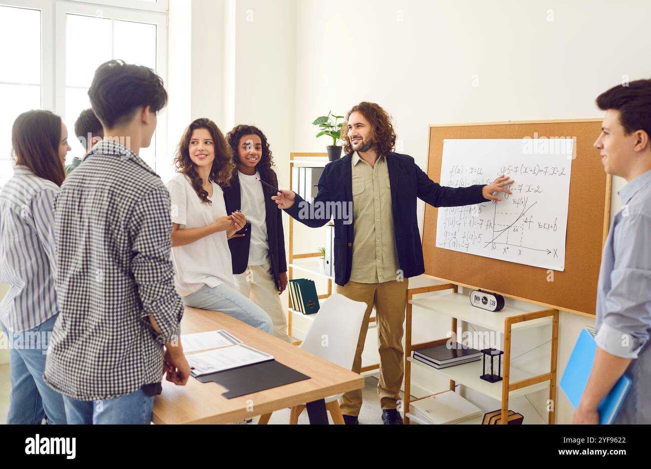 Math teacher standing by board and explaining algebraic equations to ...