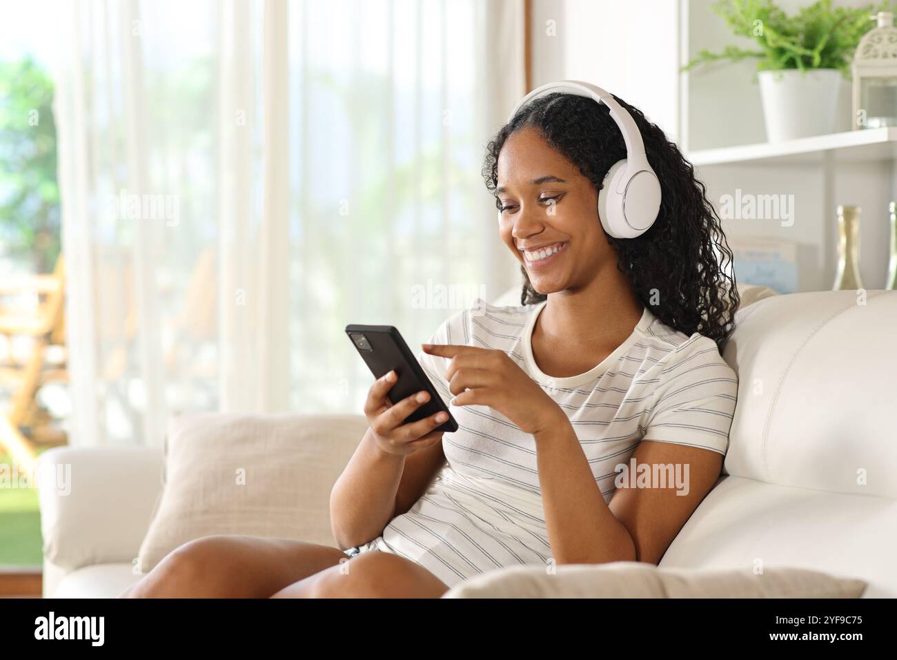 Happy black woman listening to music using phone and headphone in a ...