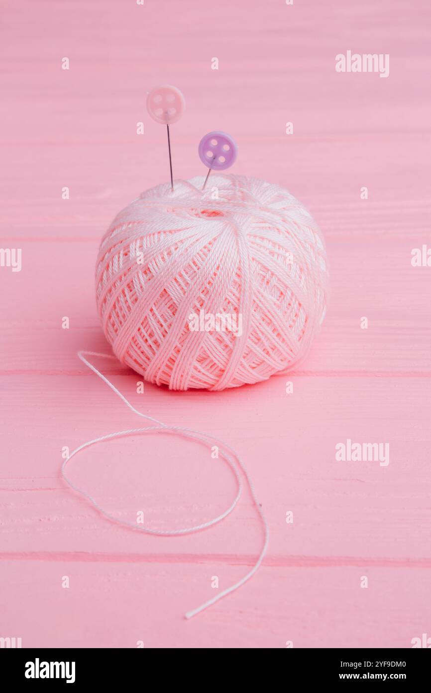 Pins are stuck into a soft pink skein of knitting thread. Needles with ...