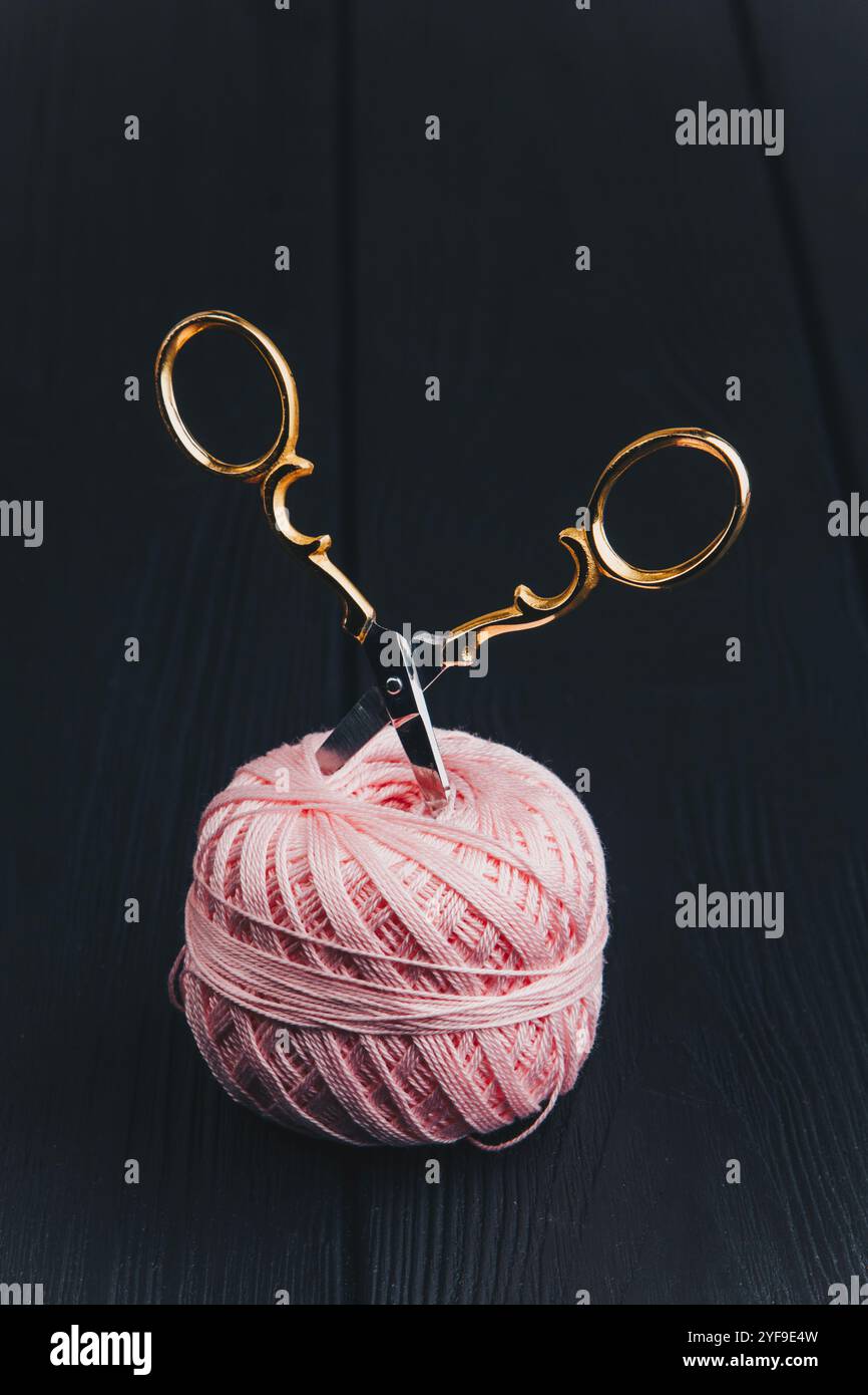 Golden steel scissors on black boards are stuck into a pink silk skein ...