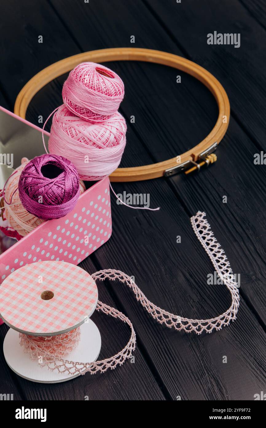 Assorted yarn and sewing tools in a pink tin box on a black wooden ...