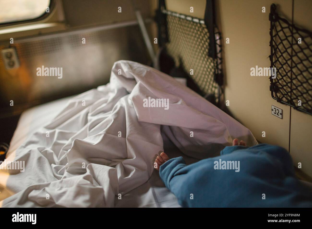 Low section of boy lying down on bed near crumpled blanket in sleeper ...