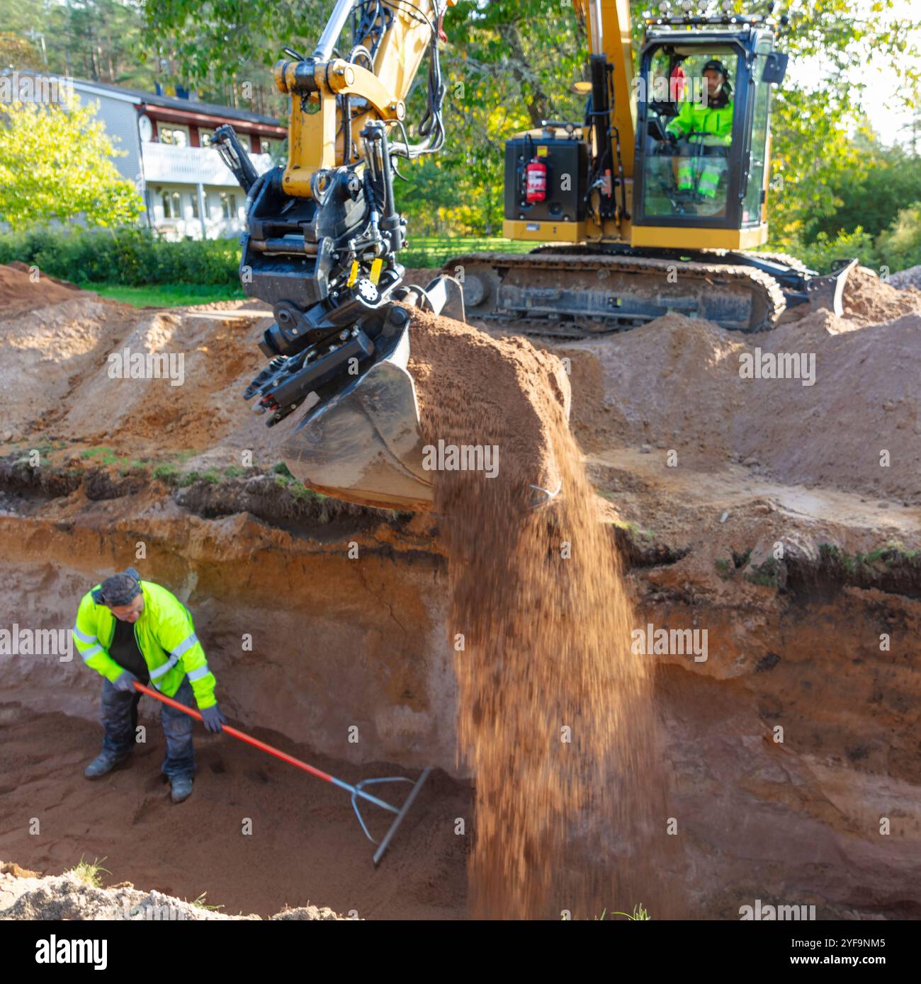 Man in tractor pouring dirt in trench while coworker using pitchfork ...