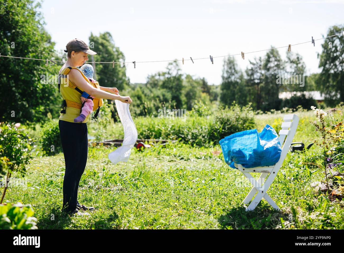 Side view of mother carrying baby while hanging laundry on clothesline ...