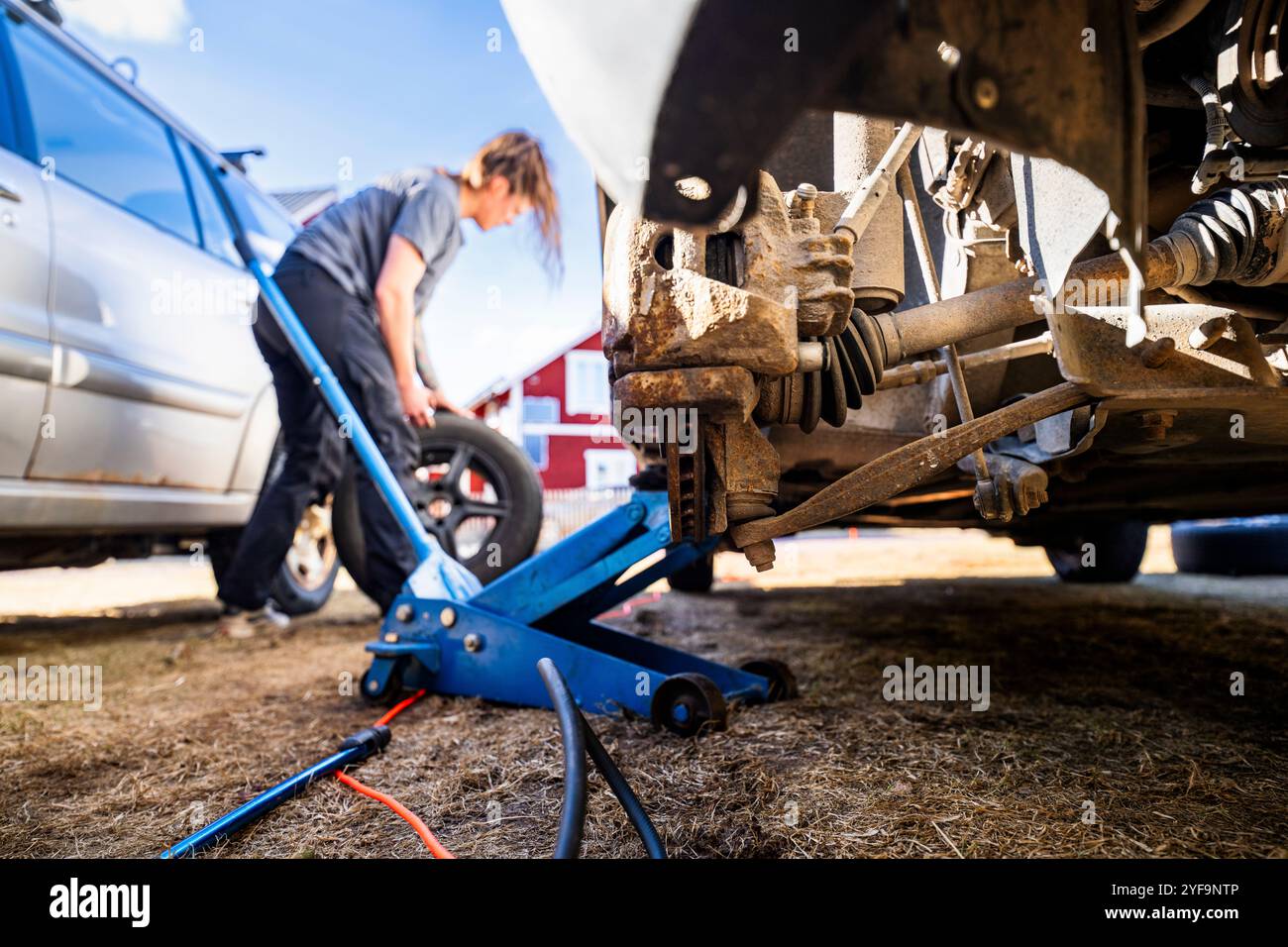 Vehicle lifted by car jack while female mechanic standing with tire on ...