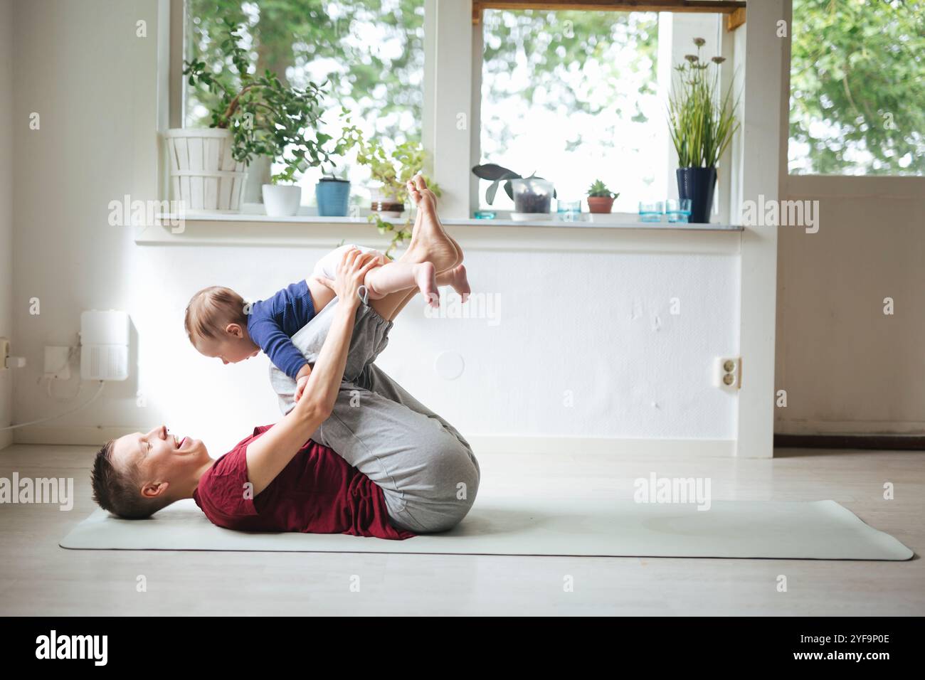 Cheerful mother balancing baby while exercising at home Stock Photo - Alamy