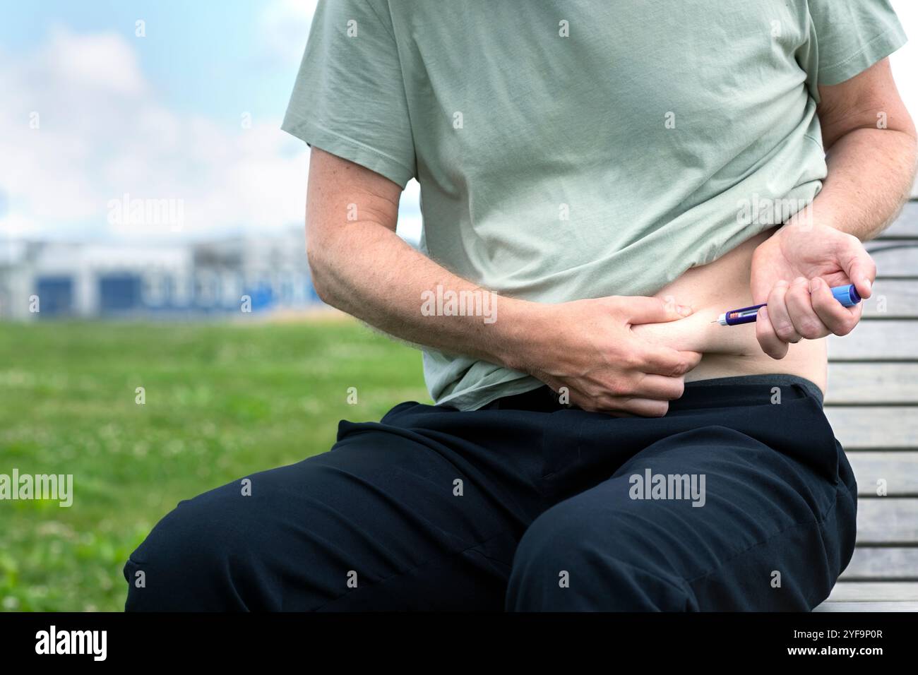 Midsection of man injecting diabetes insulin while sitting on bench at ...