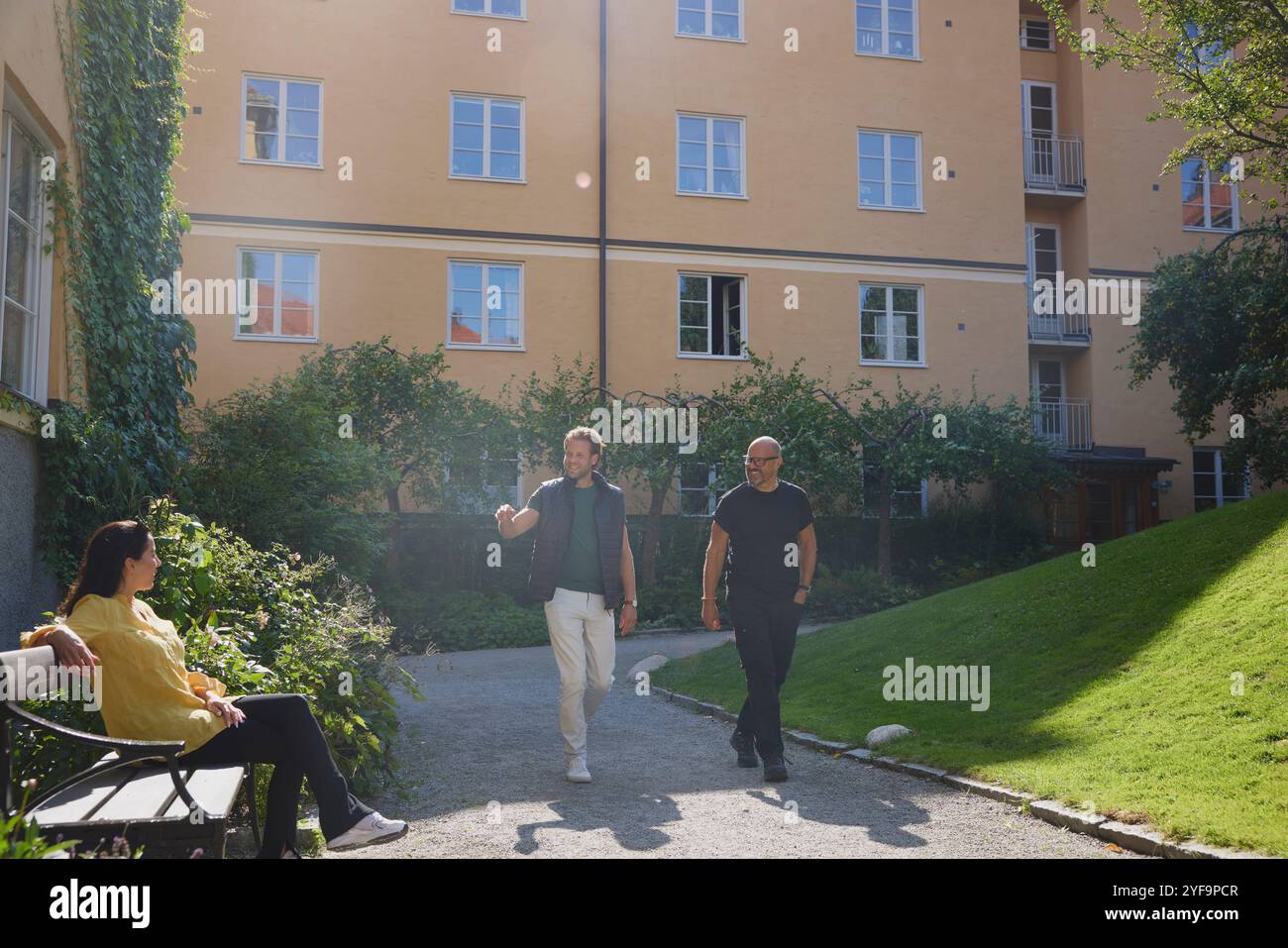 Happy male friends walking on footpath greeting female neighbor sitting ...