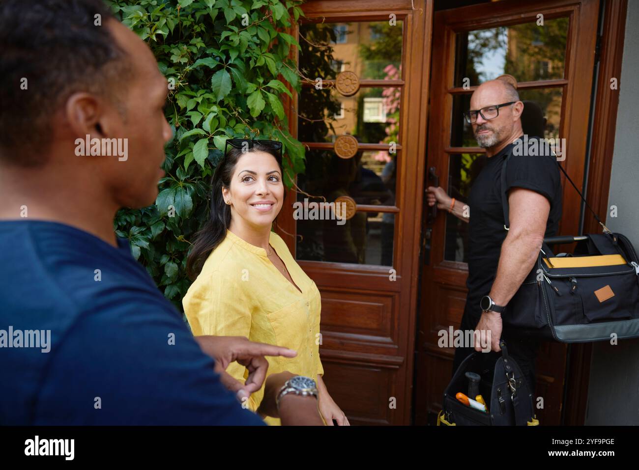 Male and female neighbors talking with repairperson opening door of ...