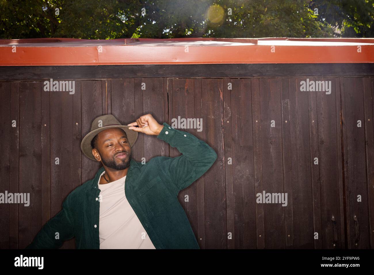 Smiling young man tipping hat while leaning on wall Stock Photo - Alamy