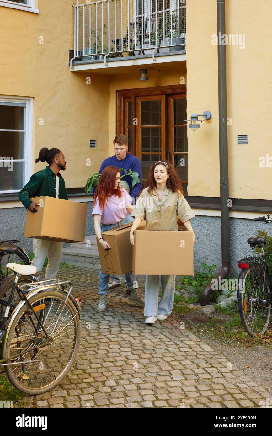 Group of friends carrying cardboard boxes while leaving from building ...